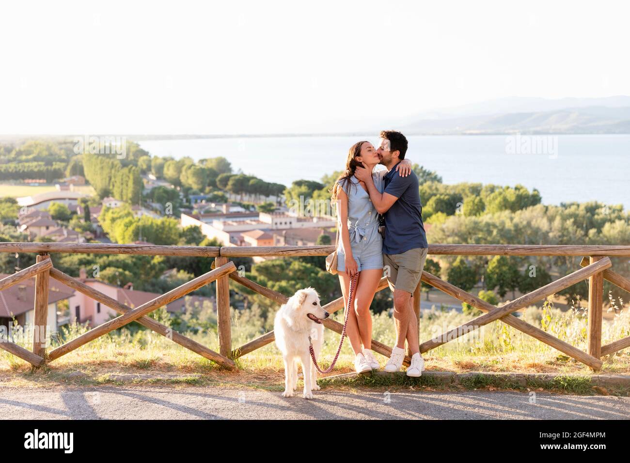 Boyfriend kissing girlfriend while leaning on railing by dog Stock ...