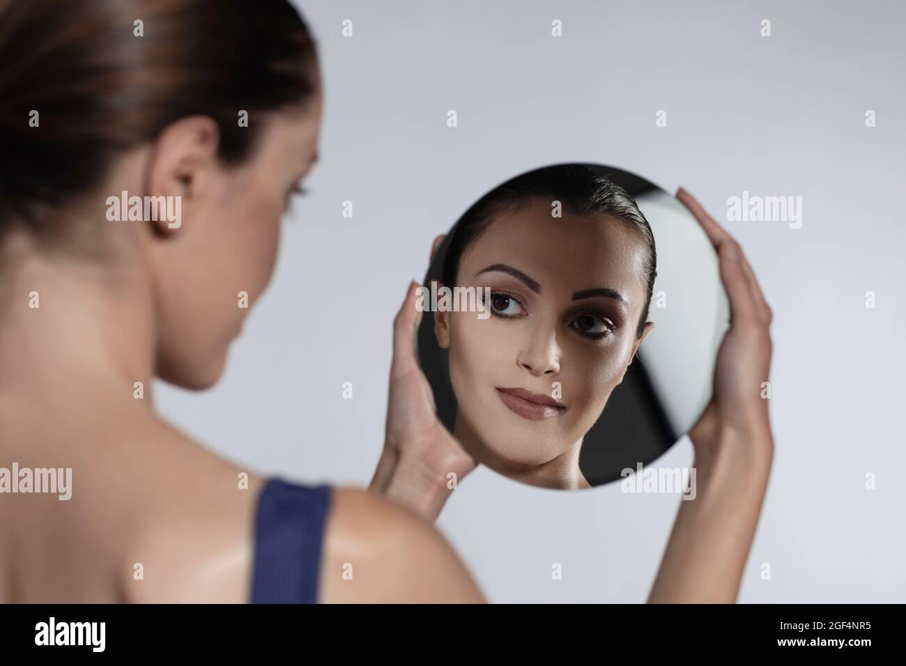 Woman looking at mirror reflection against white background Stock Photo ...