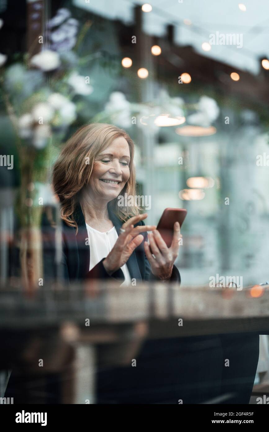 Smiling female professional text messaging through smart phone in cafe ...