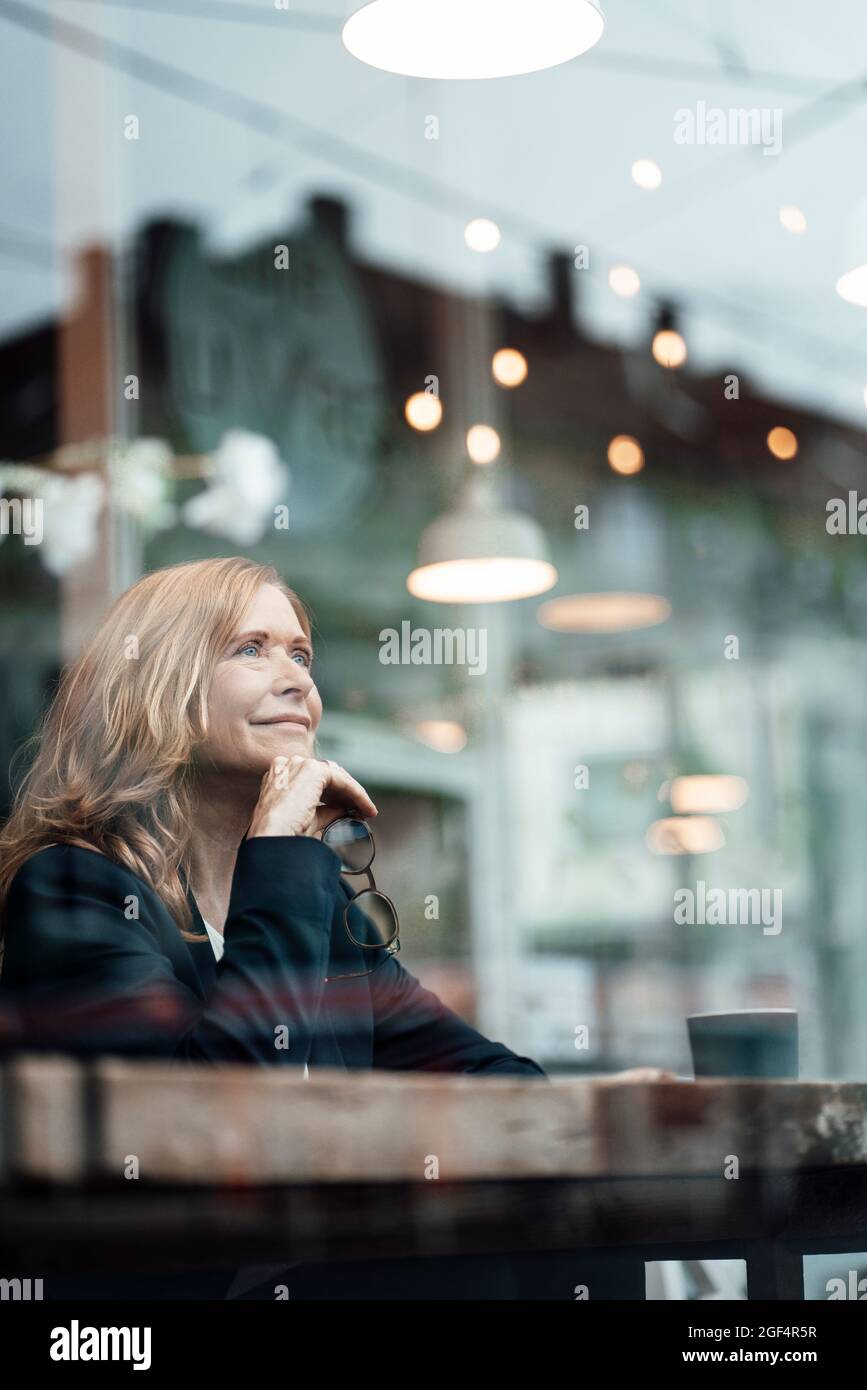 Thoughtful female professional sitting with hand on chin in cafe seen ...