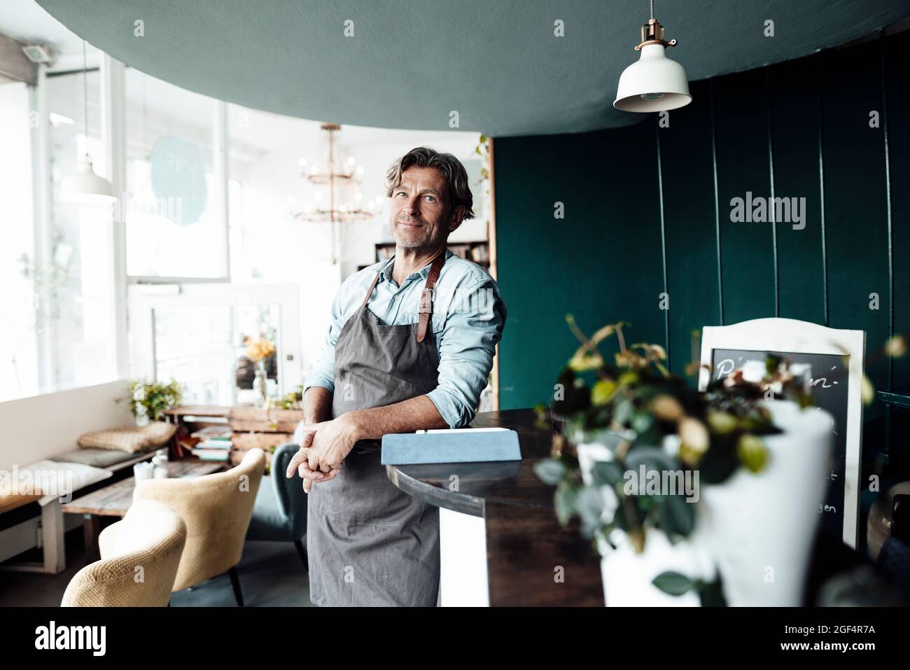 Mature male cafe owner standing while leaning on table Stock Photo - Alamy