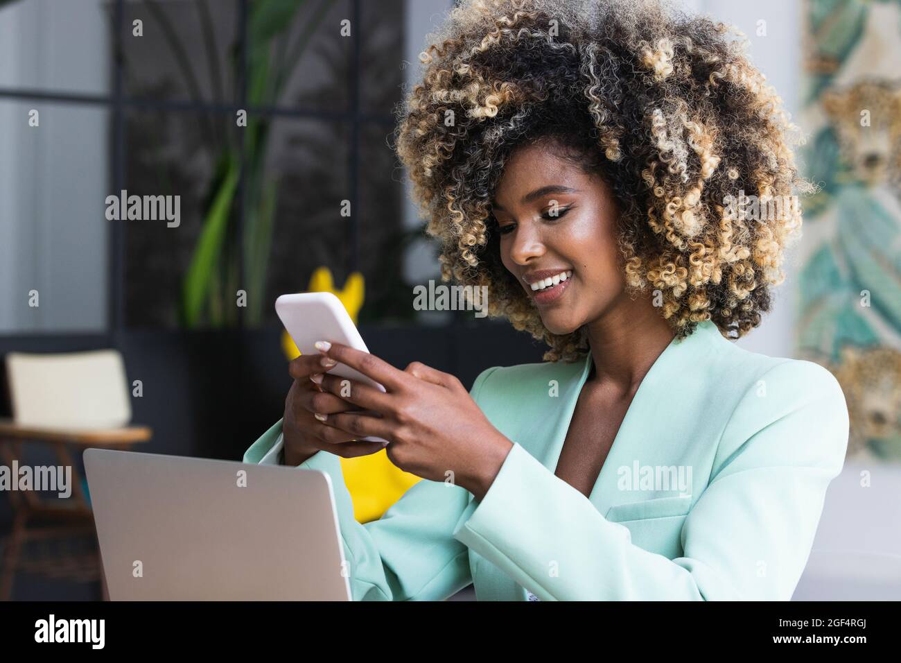 Smiling female professional with laptop using smart phone at home Stock ...