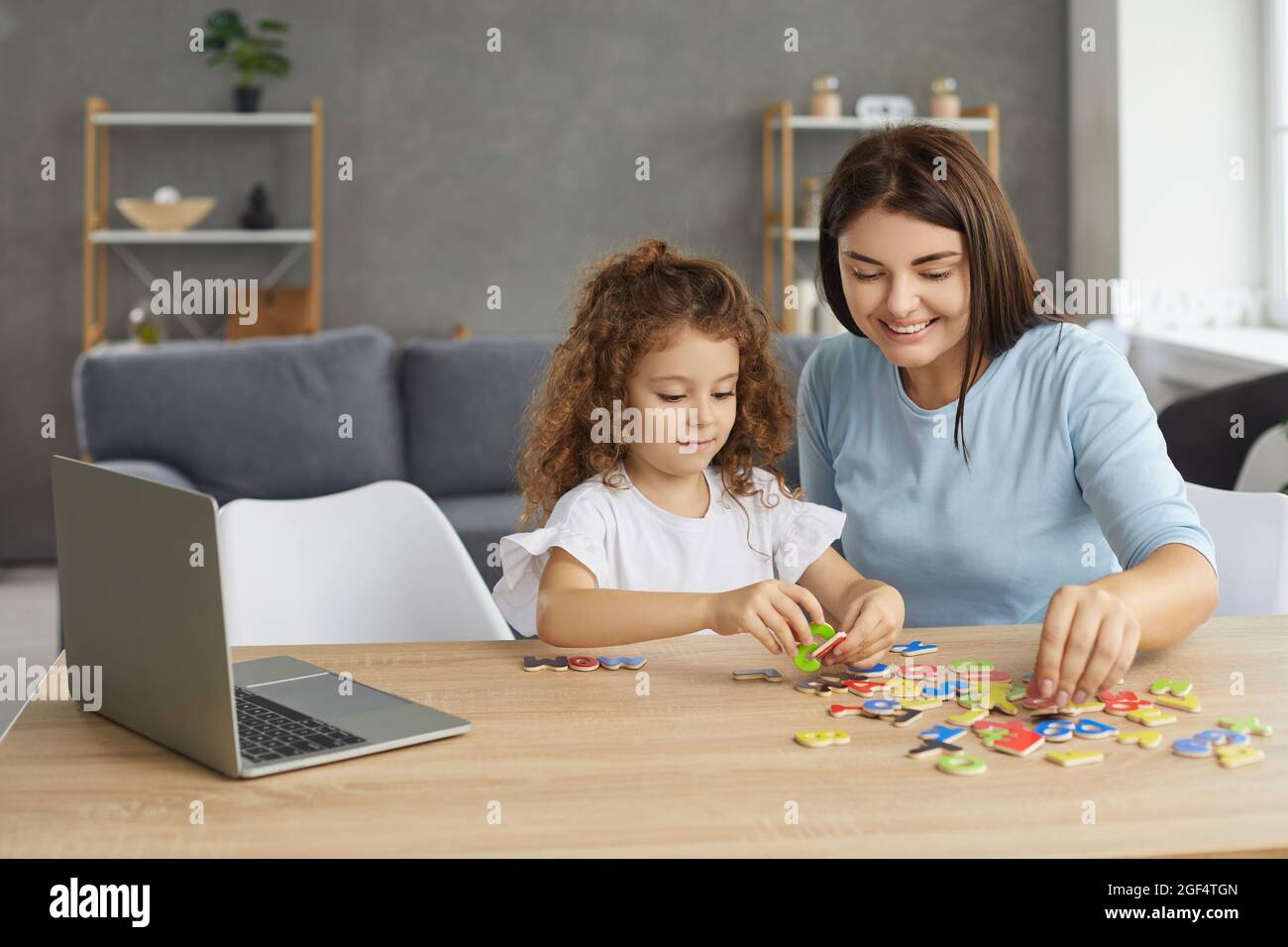Happy little girl sitting at desk and learning English with her mother ...