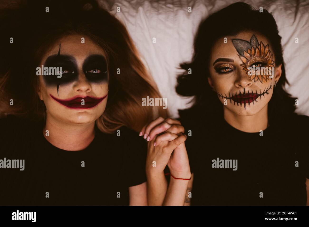 Female friends with evil make-up holding hands while lying on bed Stock ...