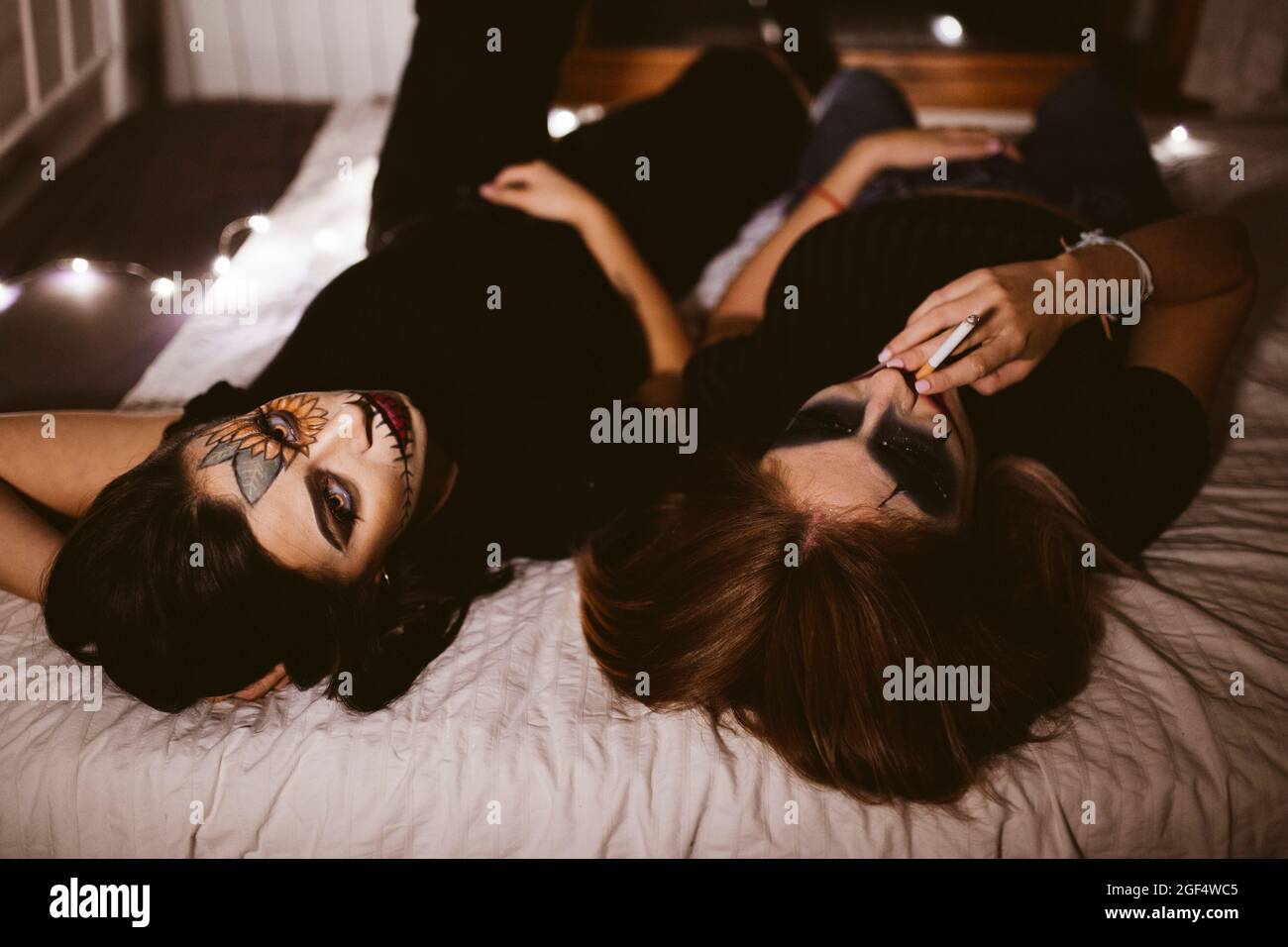 Woman smoking cigarette while lying by friend on bed at home Stock ...