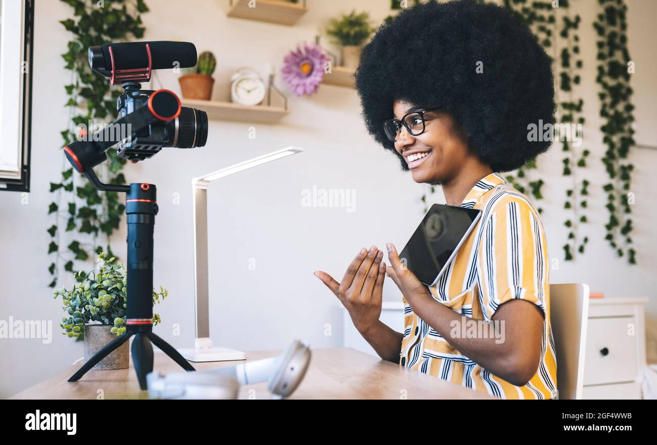 Woman showing digital tablet while filming through camera on tripod at ...