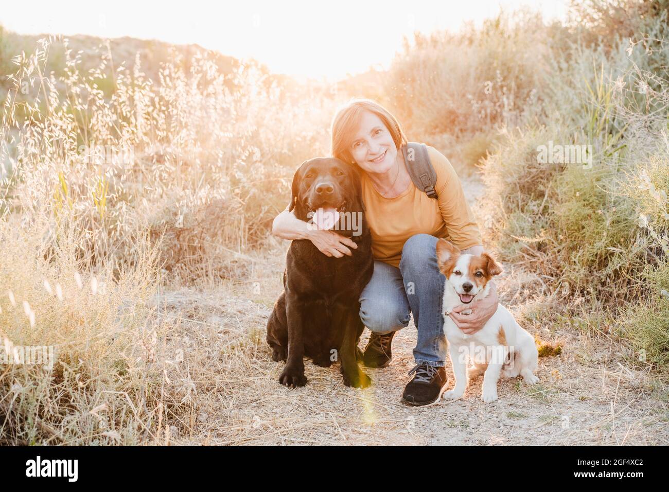 Woman embracing dogs while crouching on trail Stock Photo - Alamy