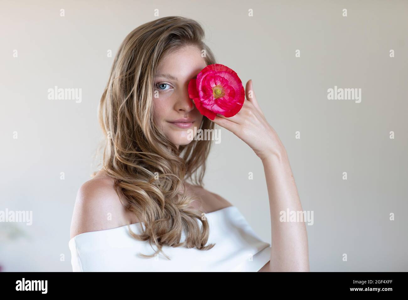 Young woman covering eye with red poppy flower Stock Photo - Alamy
