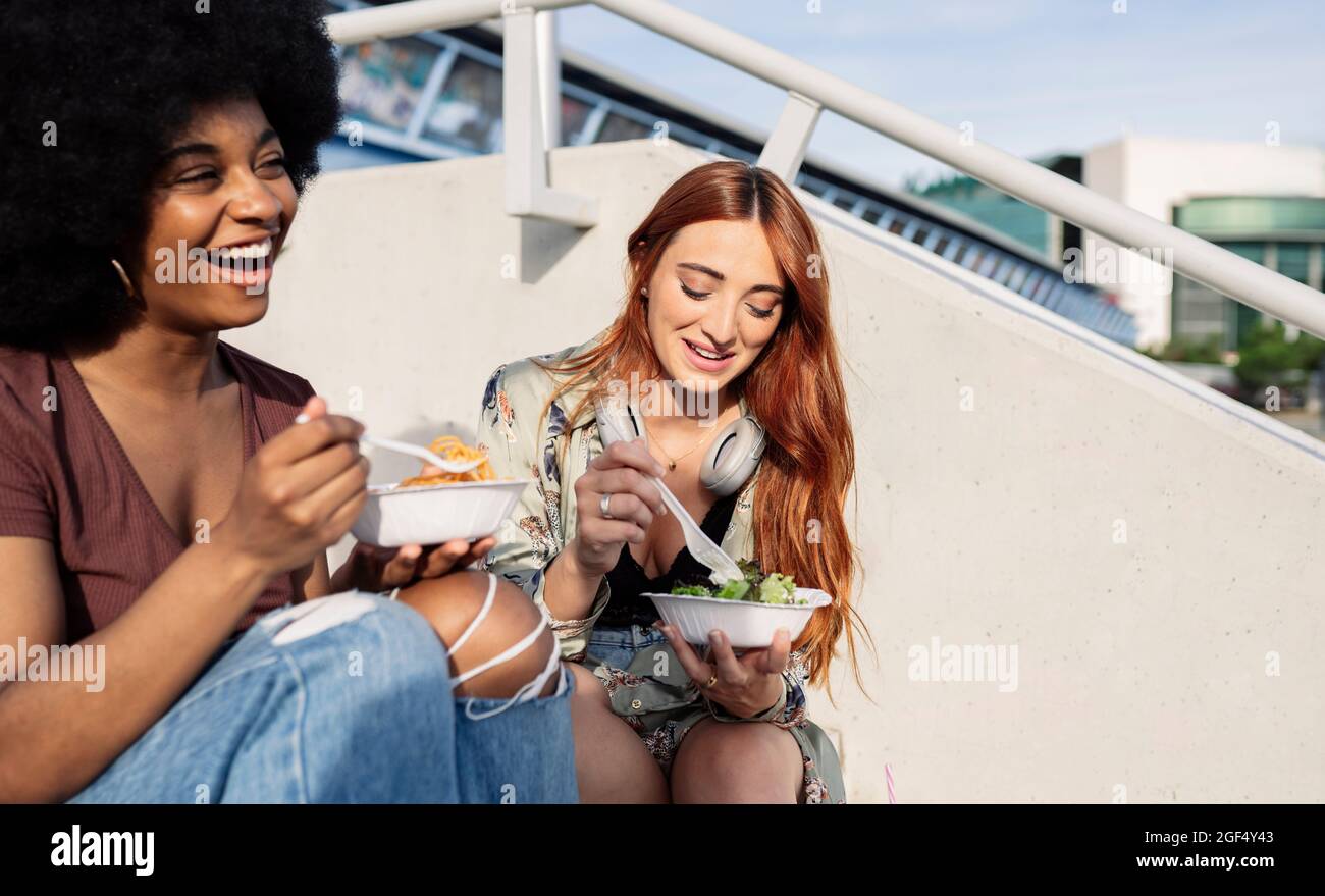 Happy young women eating while sitting on staircase Stock Photo - Alamy