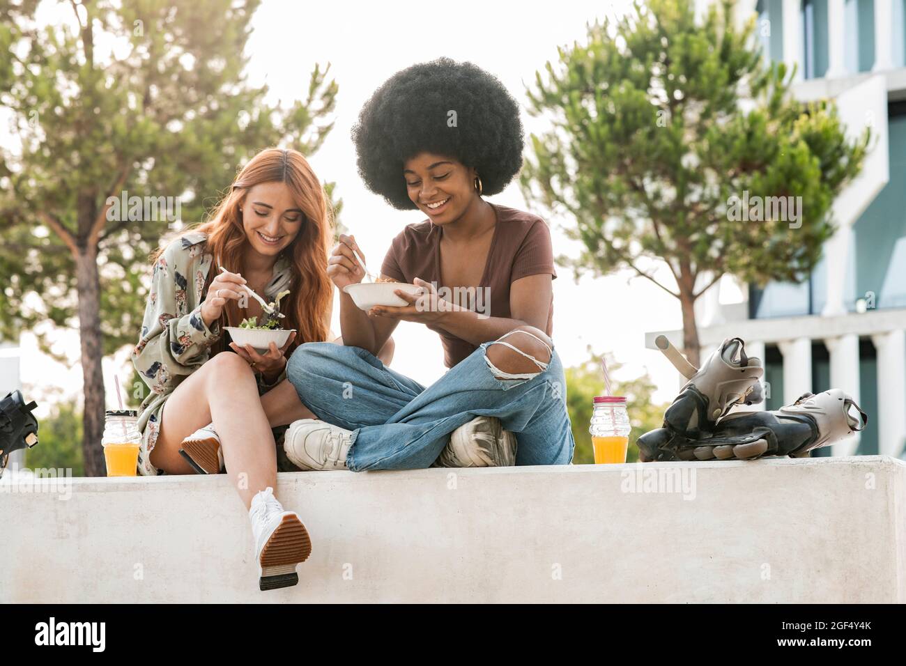 Happy female friends eating food while sitting on bench Stock Photo - Alamy