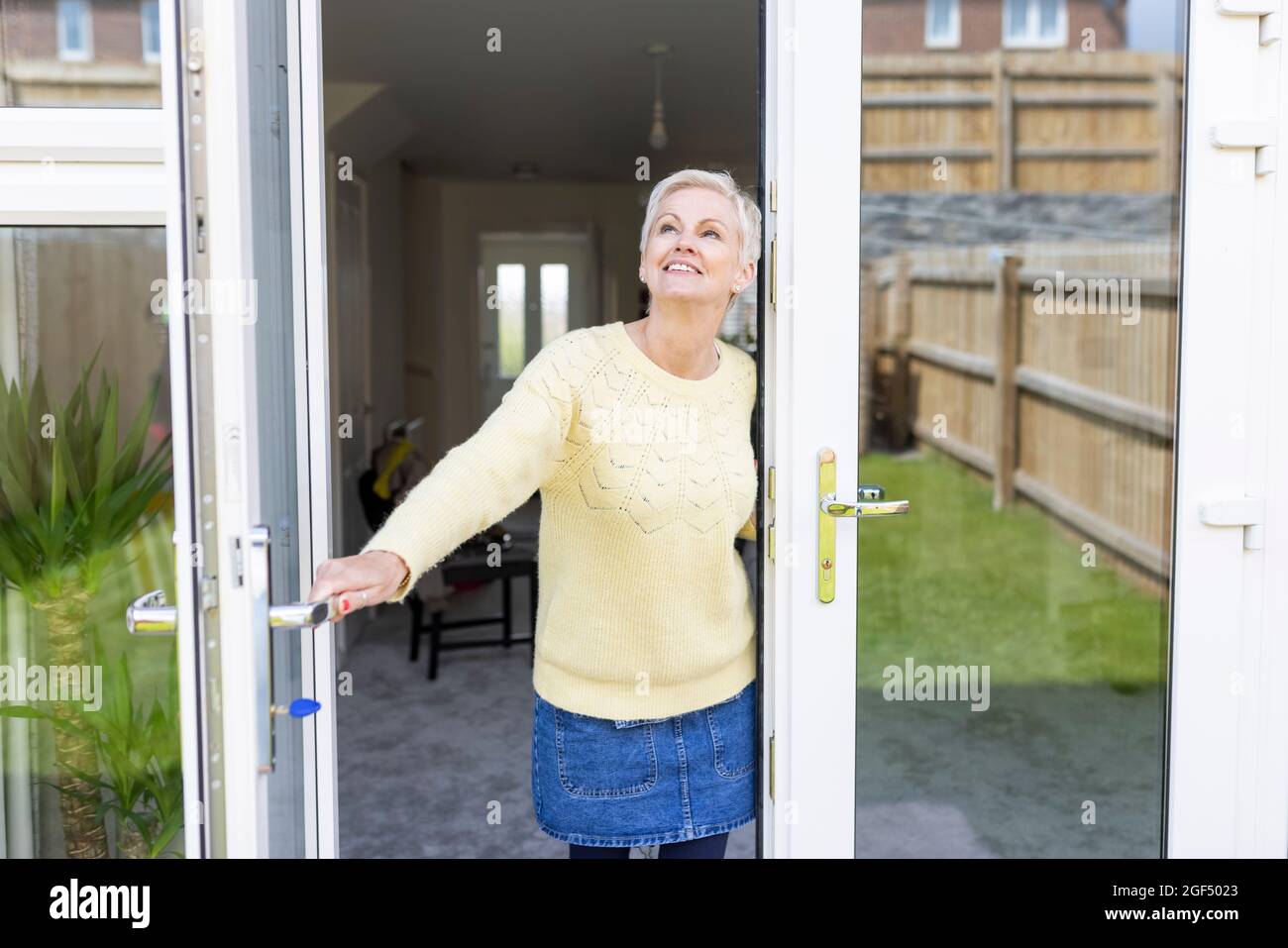 Woman looking up while opening door of house Stock Photo - Alamy