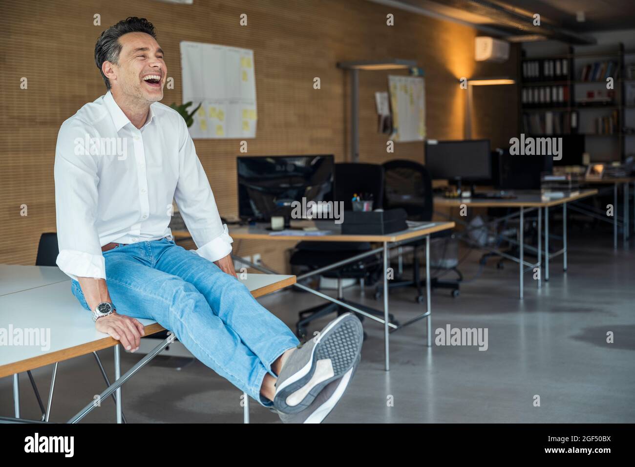Happy businessman sitting with legs crossed at ankle on desk Stock ...