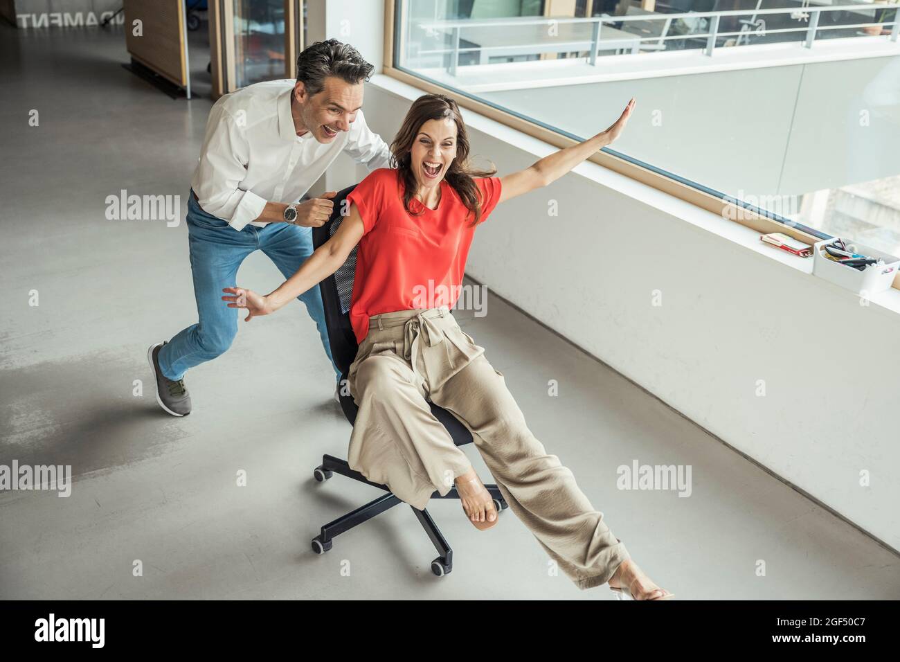 Cheerful businessman pushing female colleague sitting on office chair ...