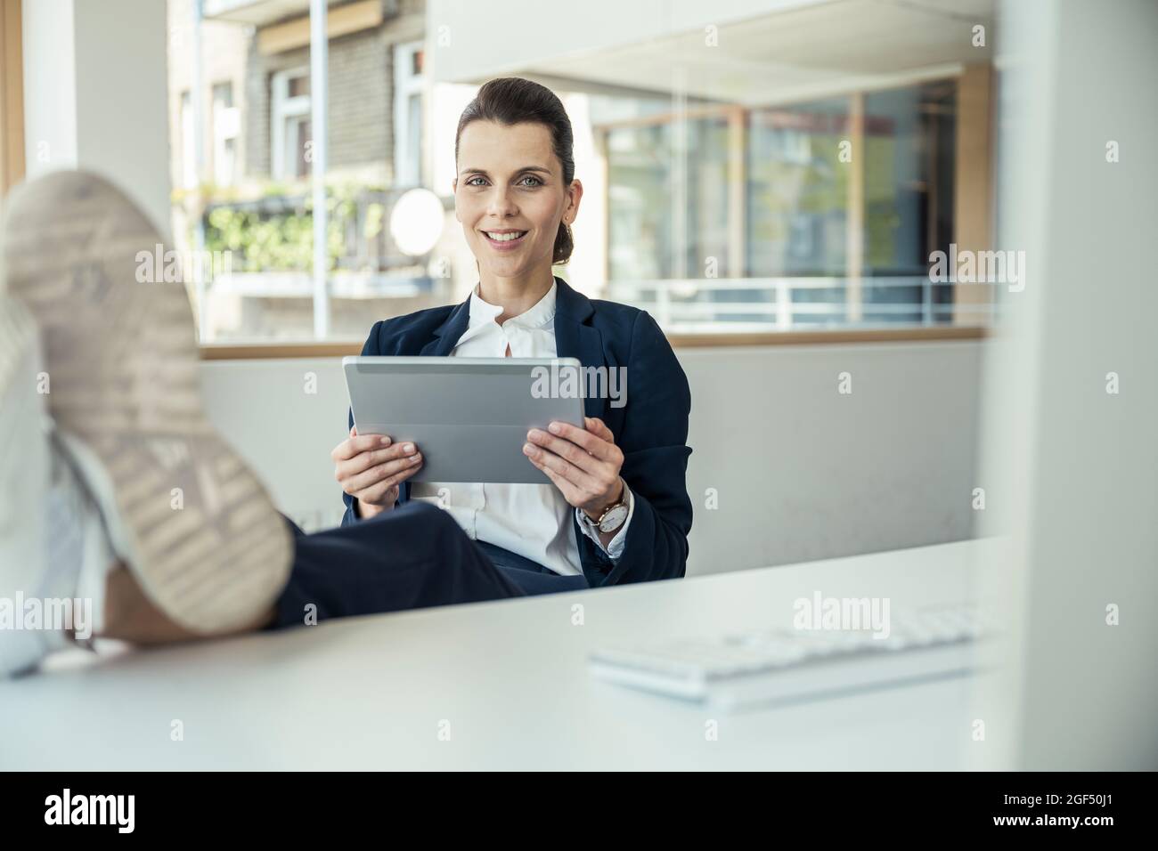 Female professional holding digital tablet while leaning leg on desk ...