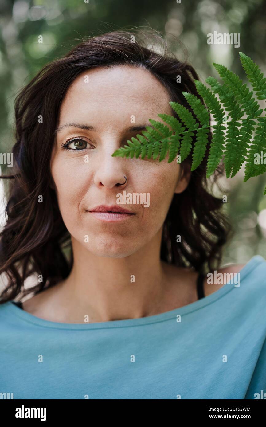 Woman covering eye with fern leaf in forest Stock Photo - Alamy