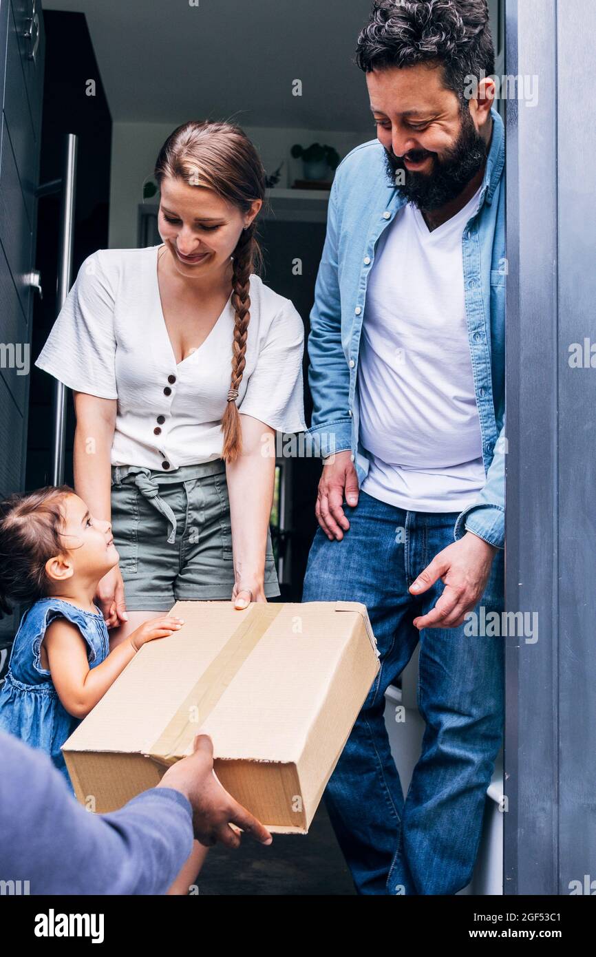 Delivery person giving package to smiling family at doorway of house ...