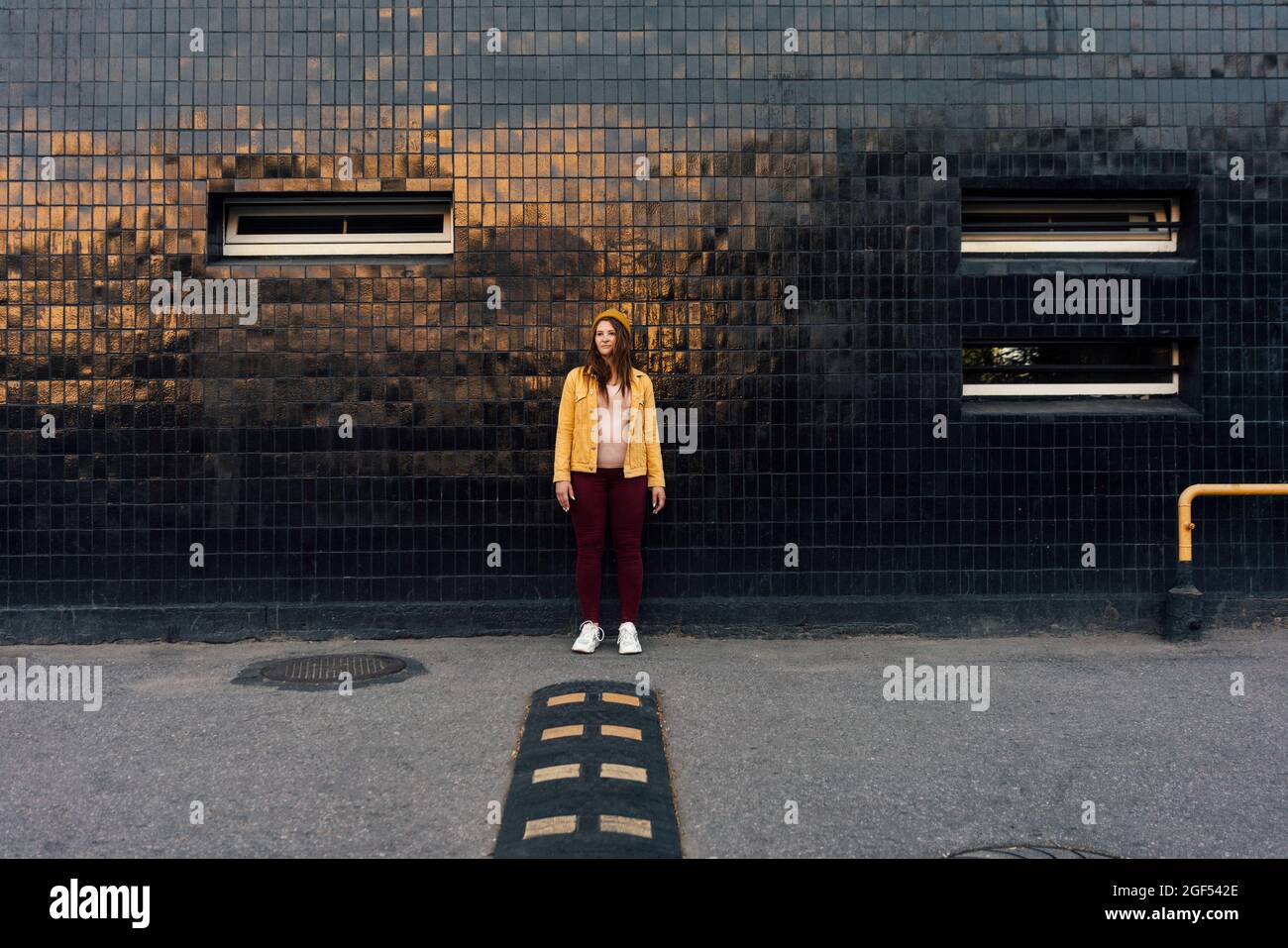 Young woman standing on footpath in front of black wall Stock Photo - Alamy