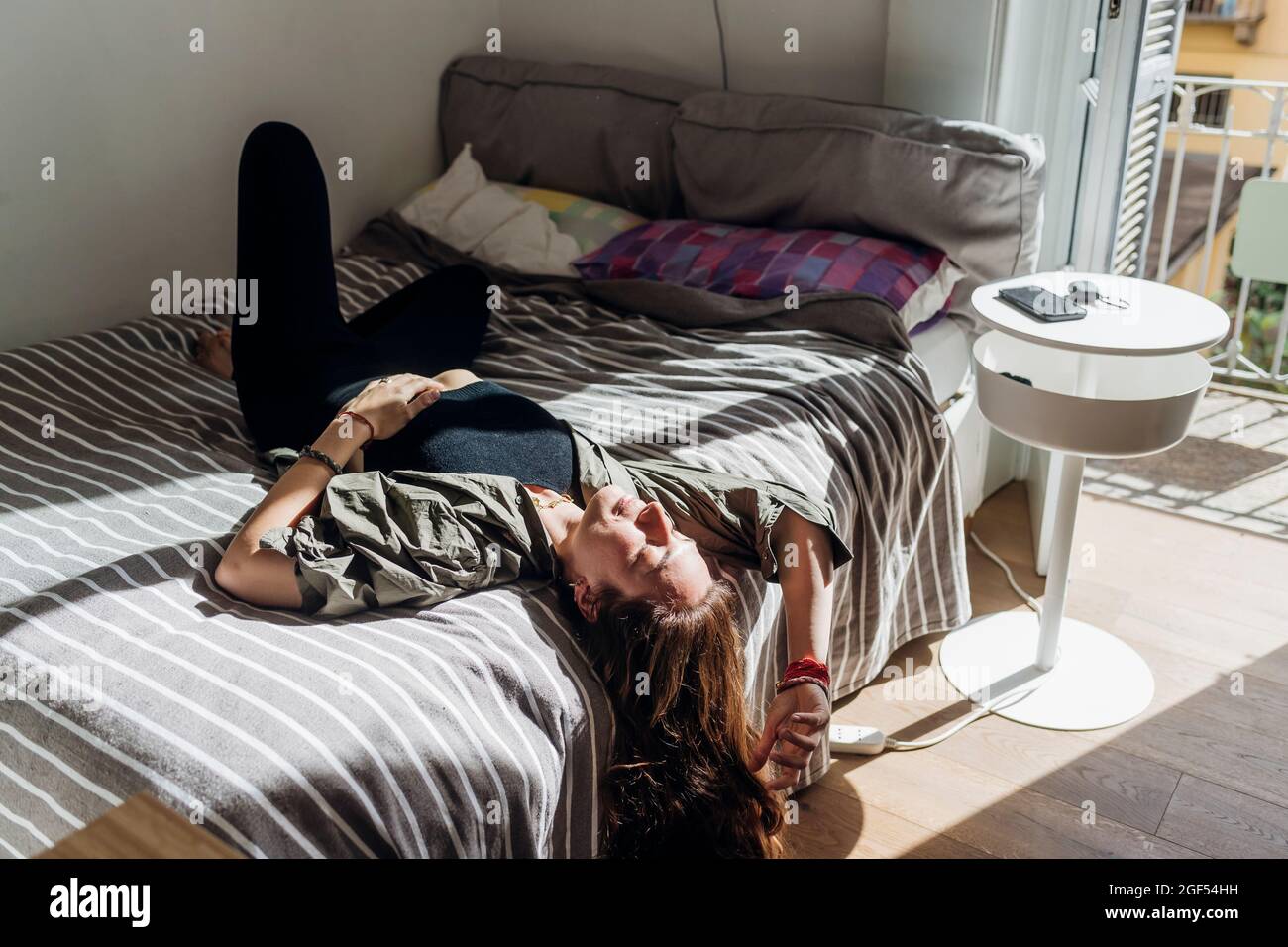 Bored woman with long brown hair lying on bed in apartment Stock Photo ...