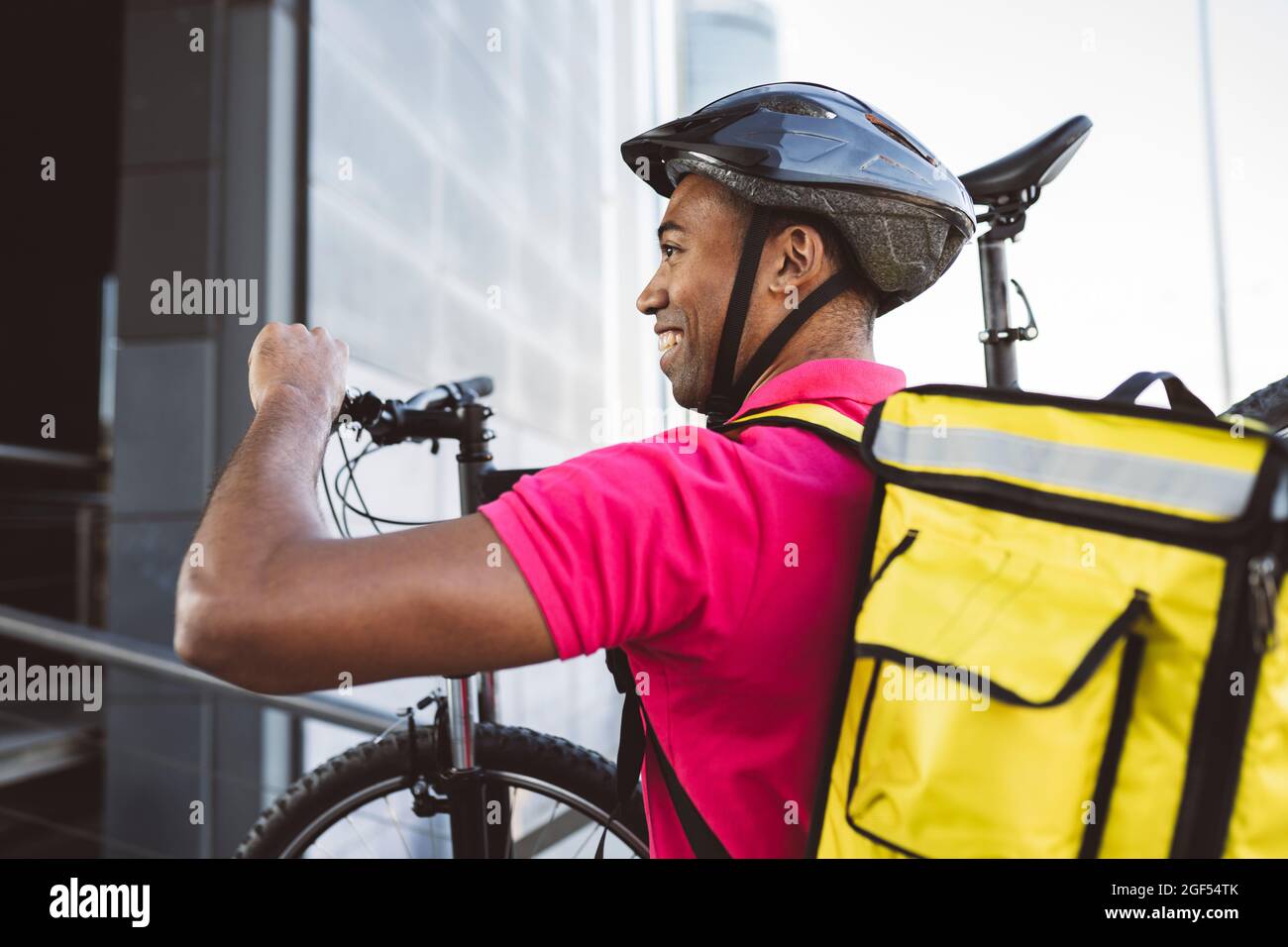 Happy delivery man wearing yellow backpack lifting bicycle Stock Photo ...