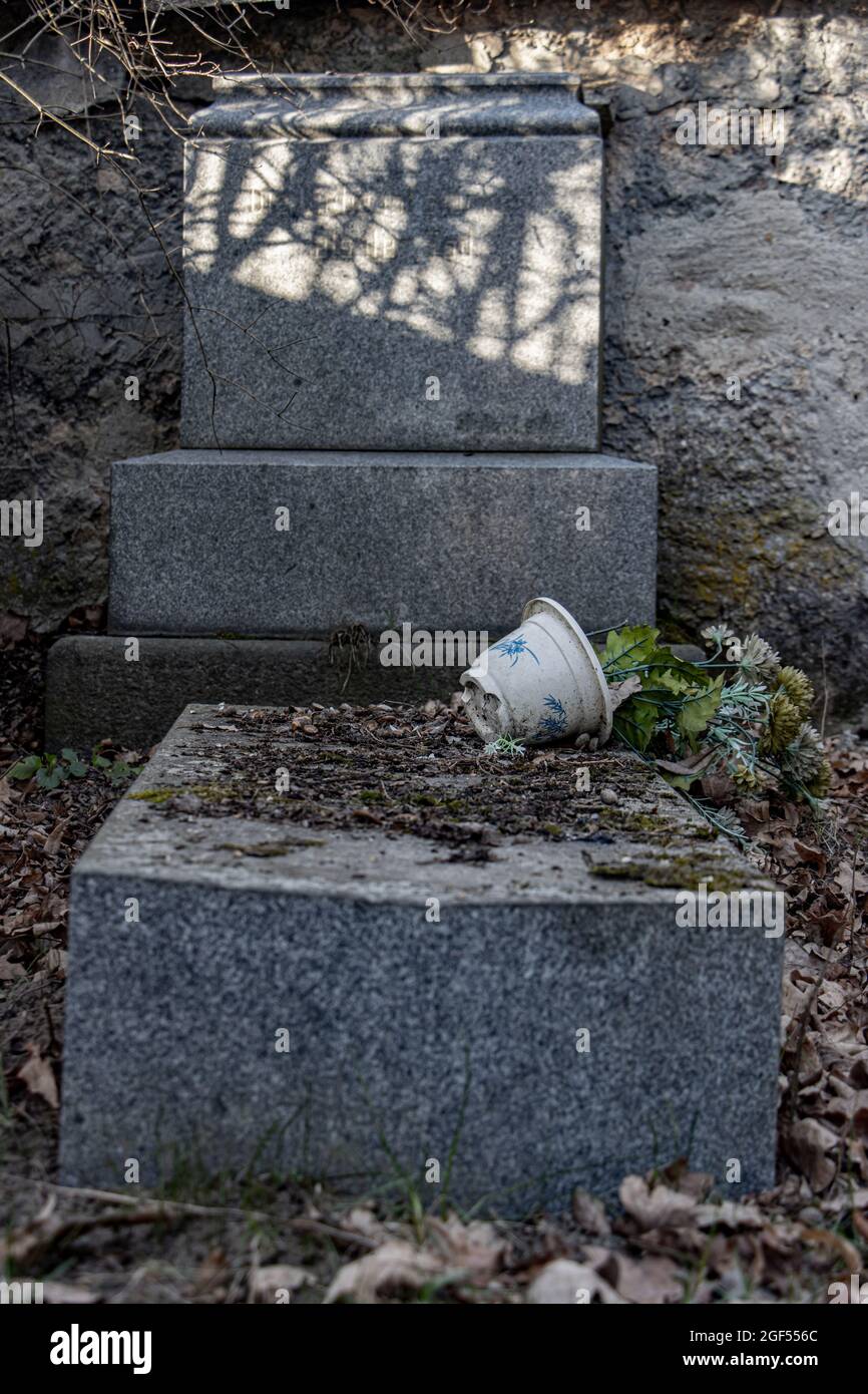 An untidy grave with a fallen flower pot on tombstone by the wall at ...