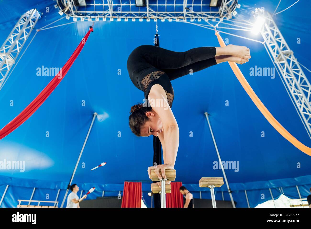 Female acrobat doing rehearsal on handstand cane with athletes in ...