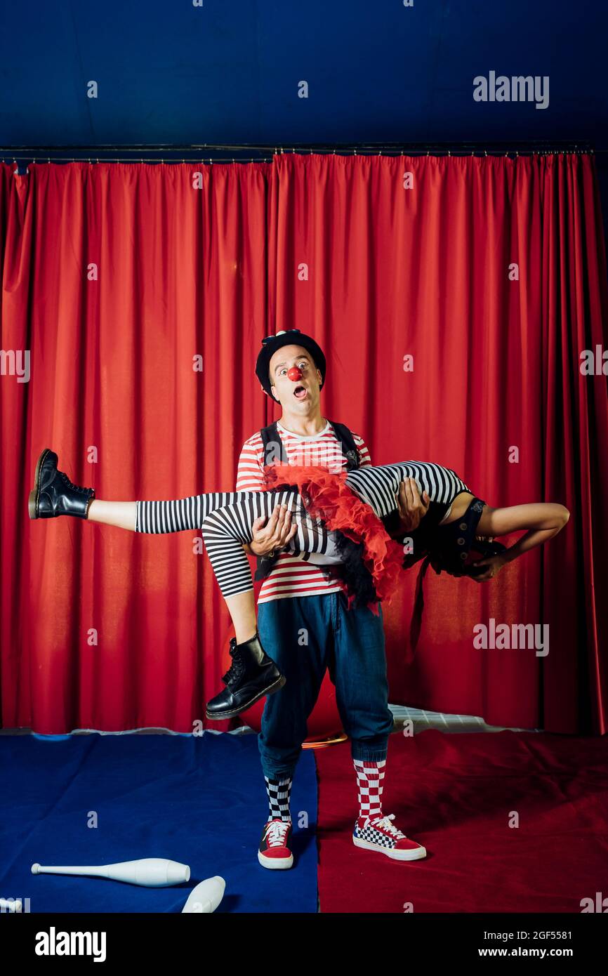 Male clown with mouth open carrying female performer on stage in circus ...