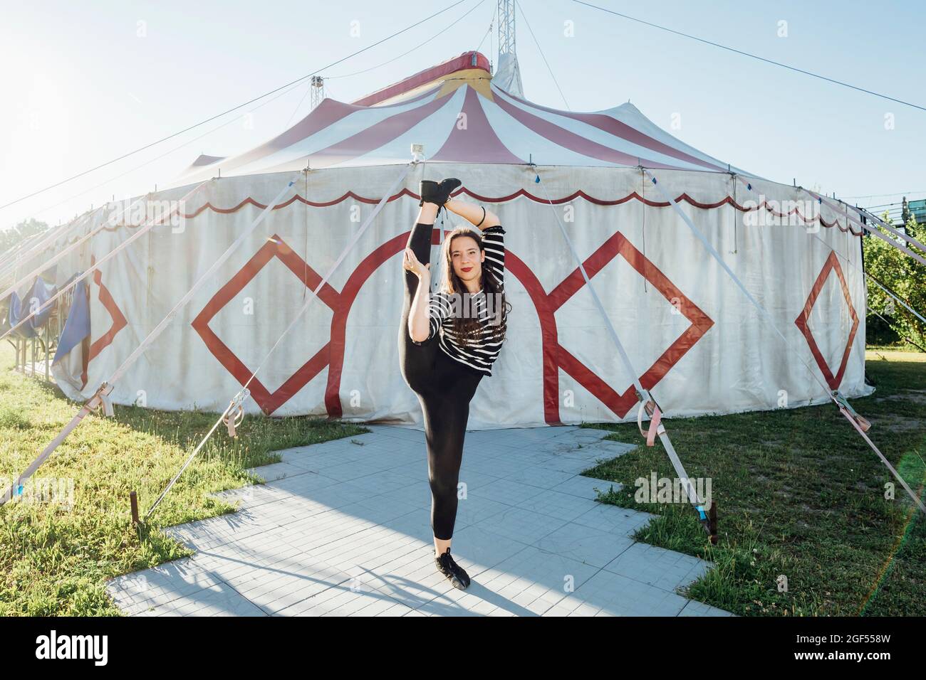 Female acrobat stretching while standing on one leg outside circus ...