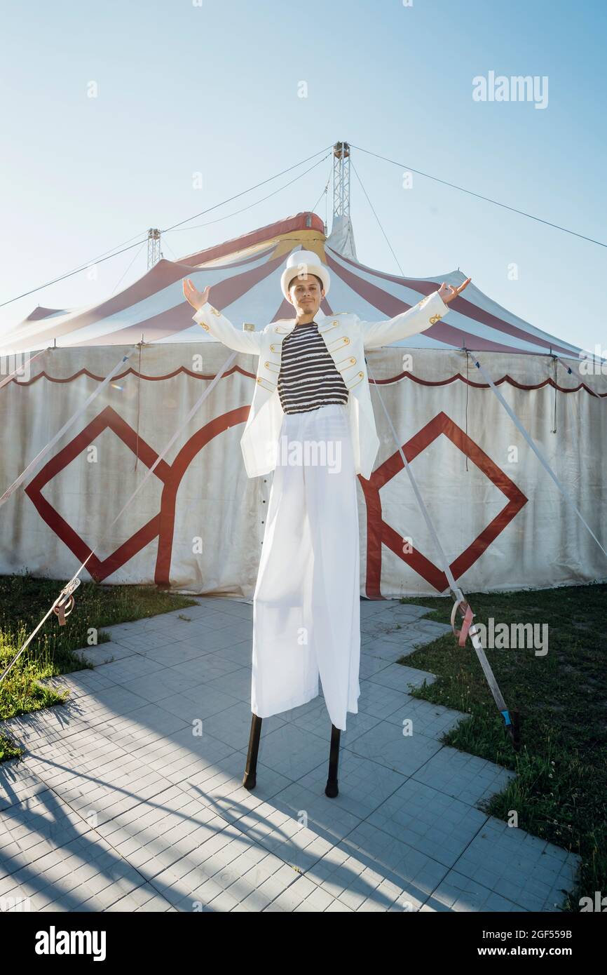 Male circus performer with arms outstretched standing with stilts on ...