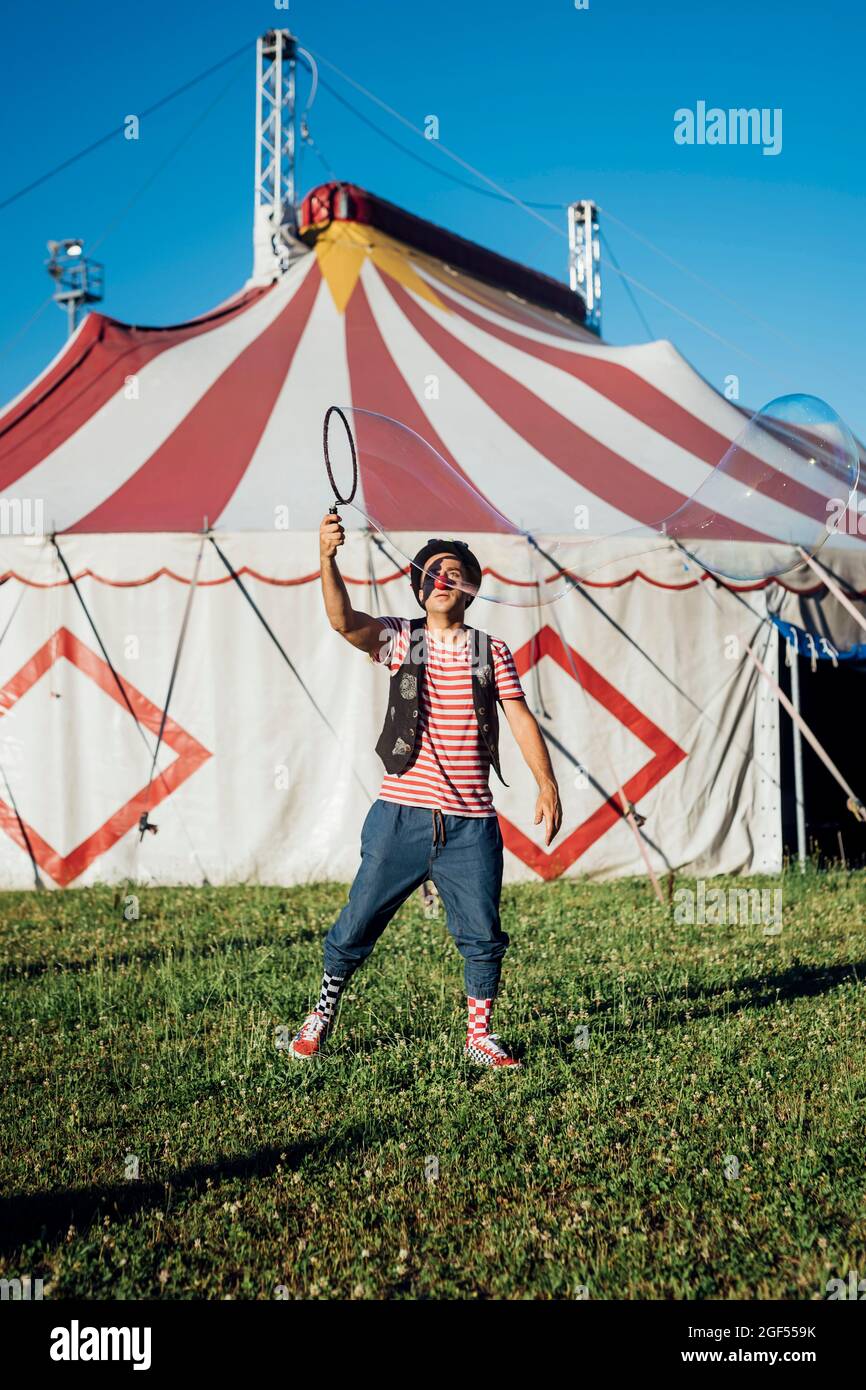 Male artist holding bubble wand while standing in front of circus tent ...