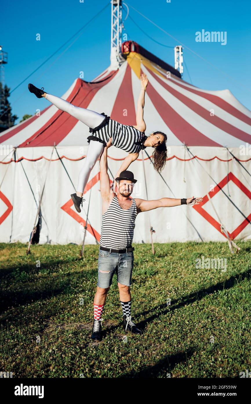 Muscular male acrobat lifting female performer while standing on meadow ...