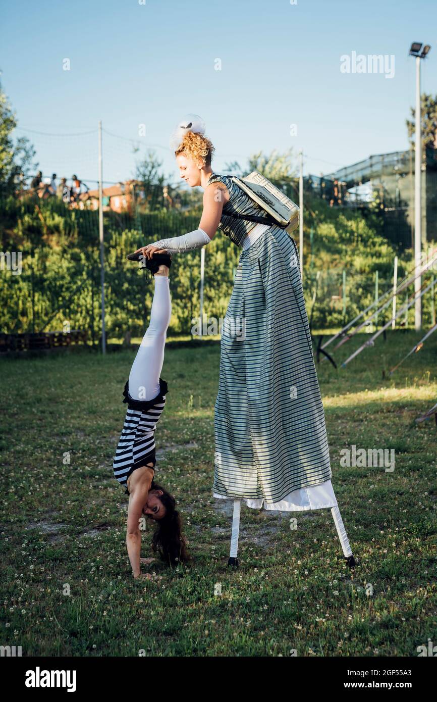 Female artist helping acrobat doing handstand on meadow Stock Photo - Alamy