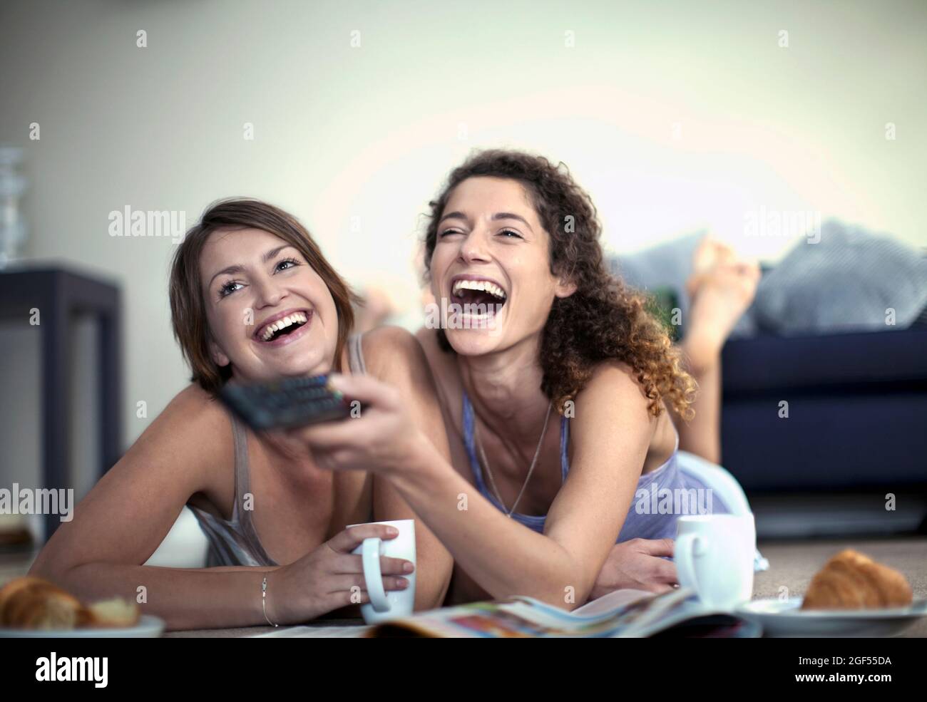 Cheerful woman changing channels with remote control while watching TV ...