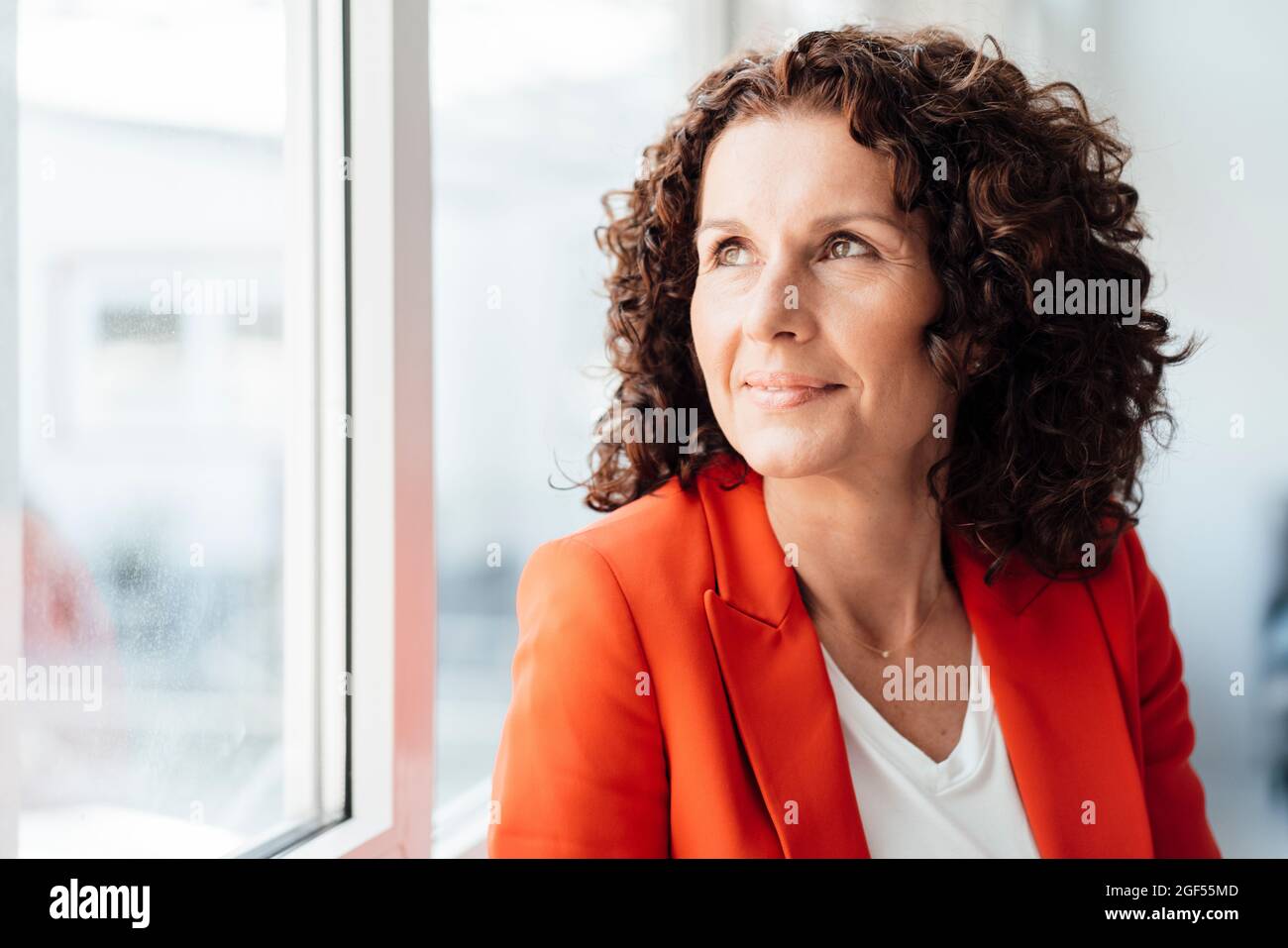 Curly haired businesswoman looking through window while contemplating ...
