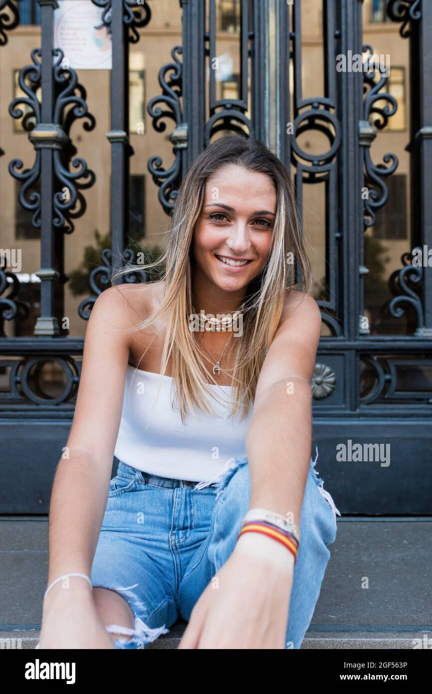 Young beautiful blond woman sitting in front of metal gate Stock Photo ...