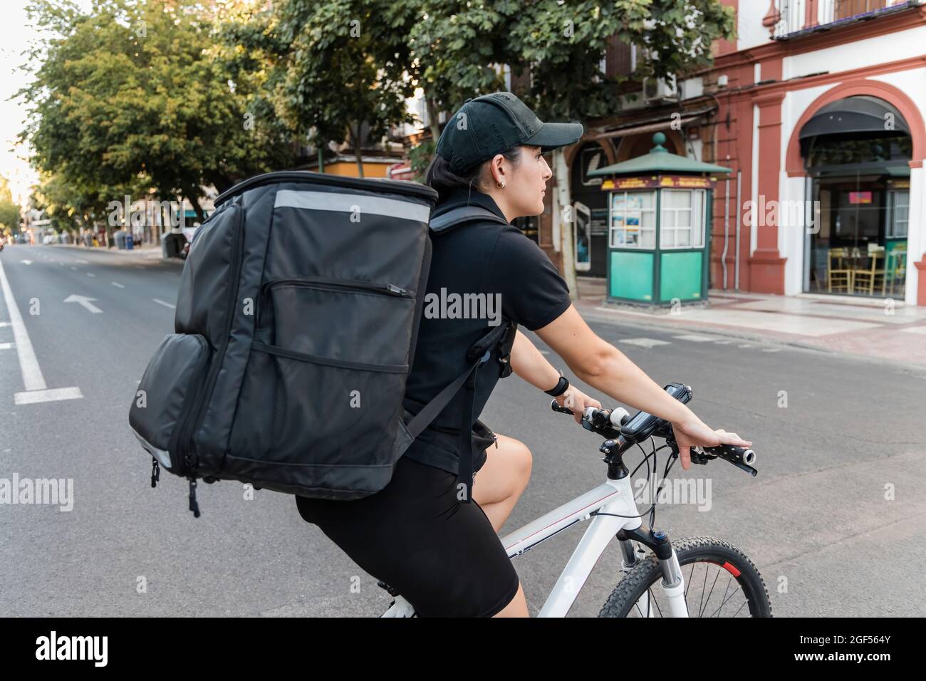 Female delivery person with backpack riding cycle on road Stock Photo ...