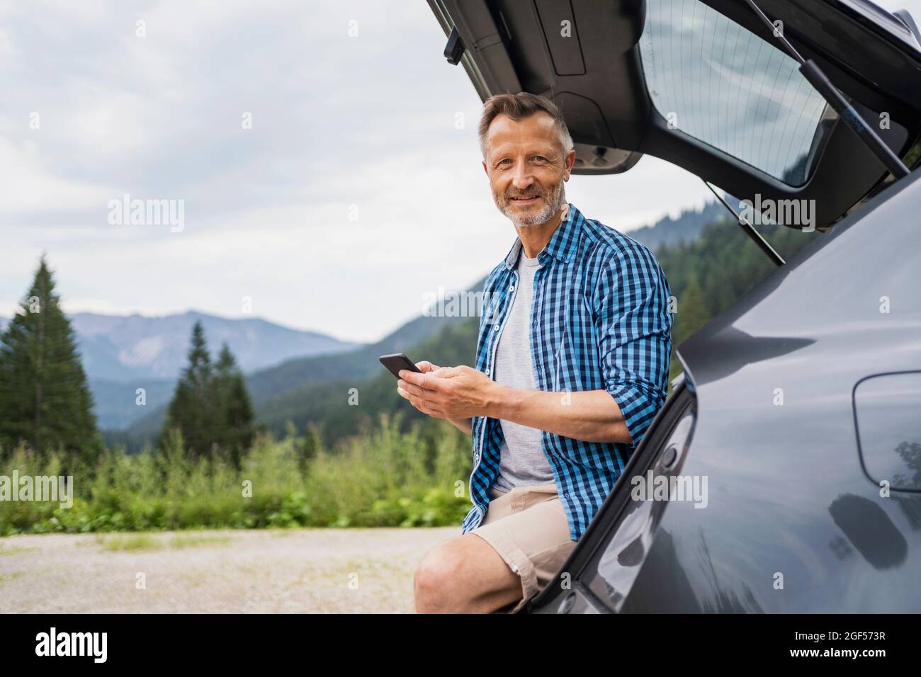 Mature man holding mobile phone while sitting in car trunk Stock Photo ...