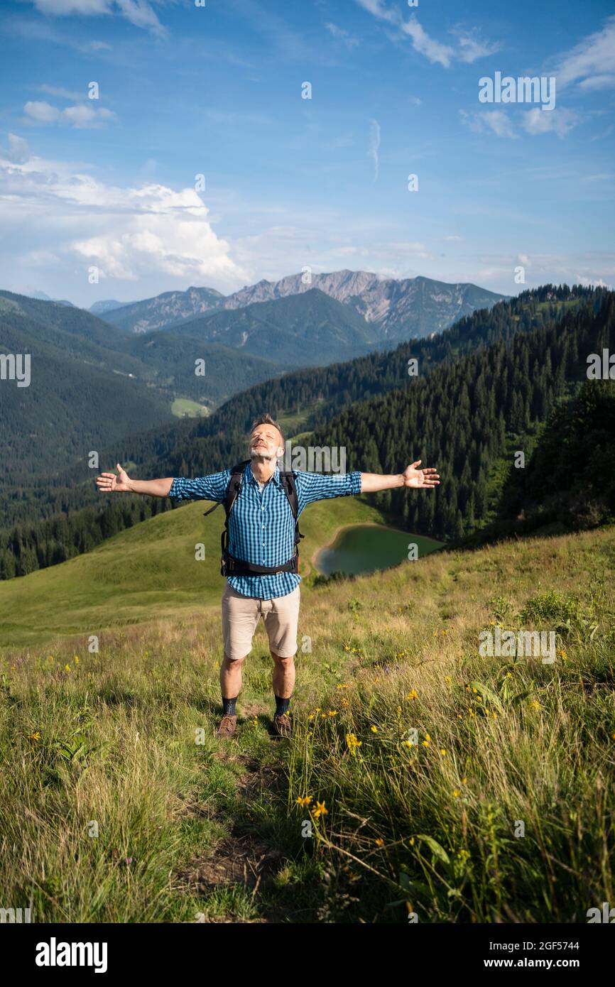 Male hiker with arms outstretched standing at meadow Stock Photo - Alamy
