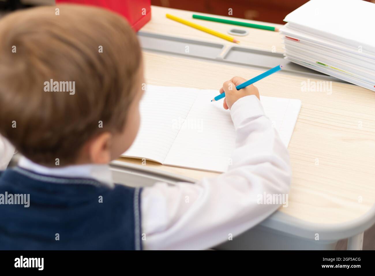 A cute boy first grader in a school uniform does homework while sitting ...
