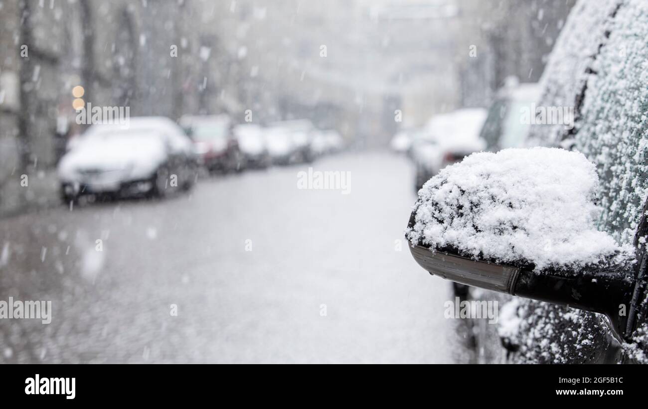 Snowflakes fall on a car mirror on a winter city street. Snowfall or ...