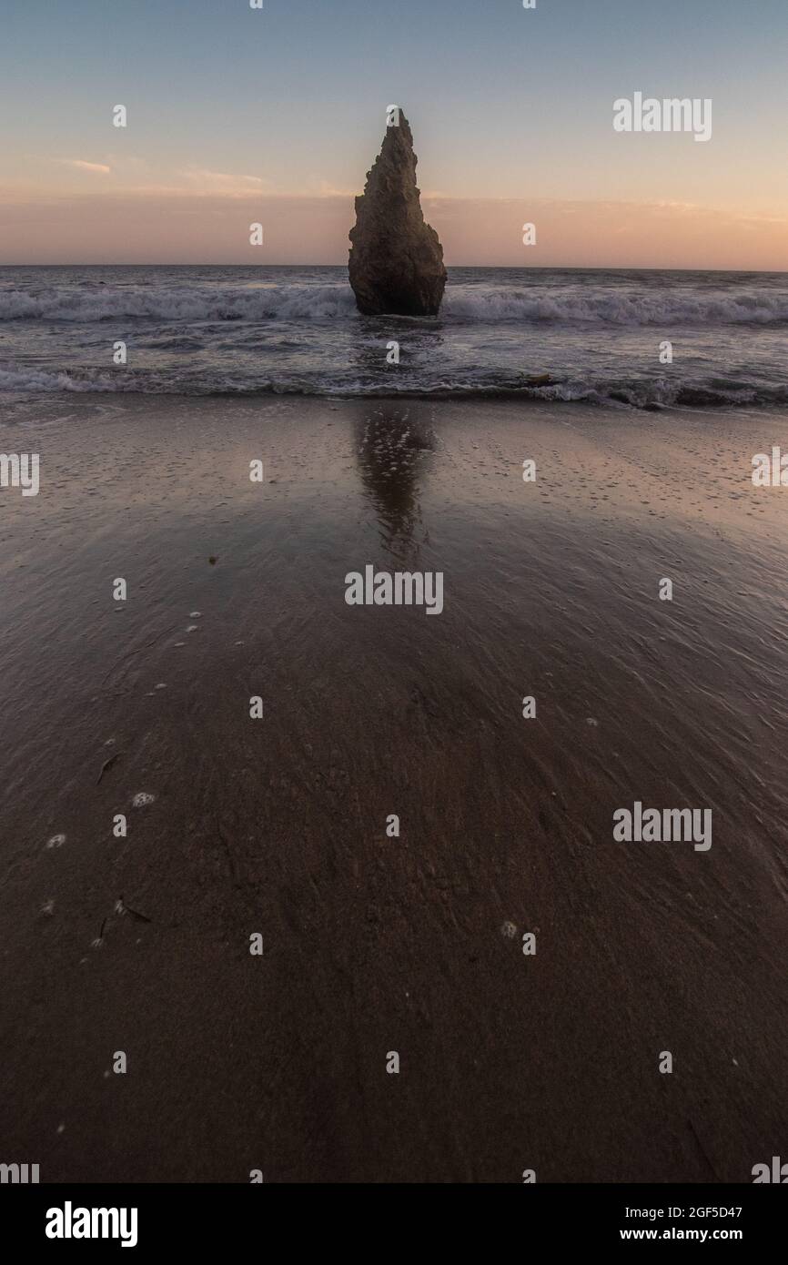 A wide angle vertical of a tall pointy rock off the shore reflected in ...