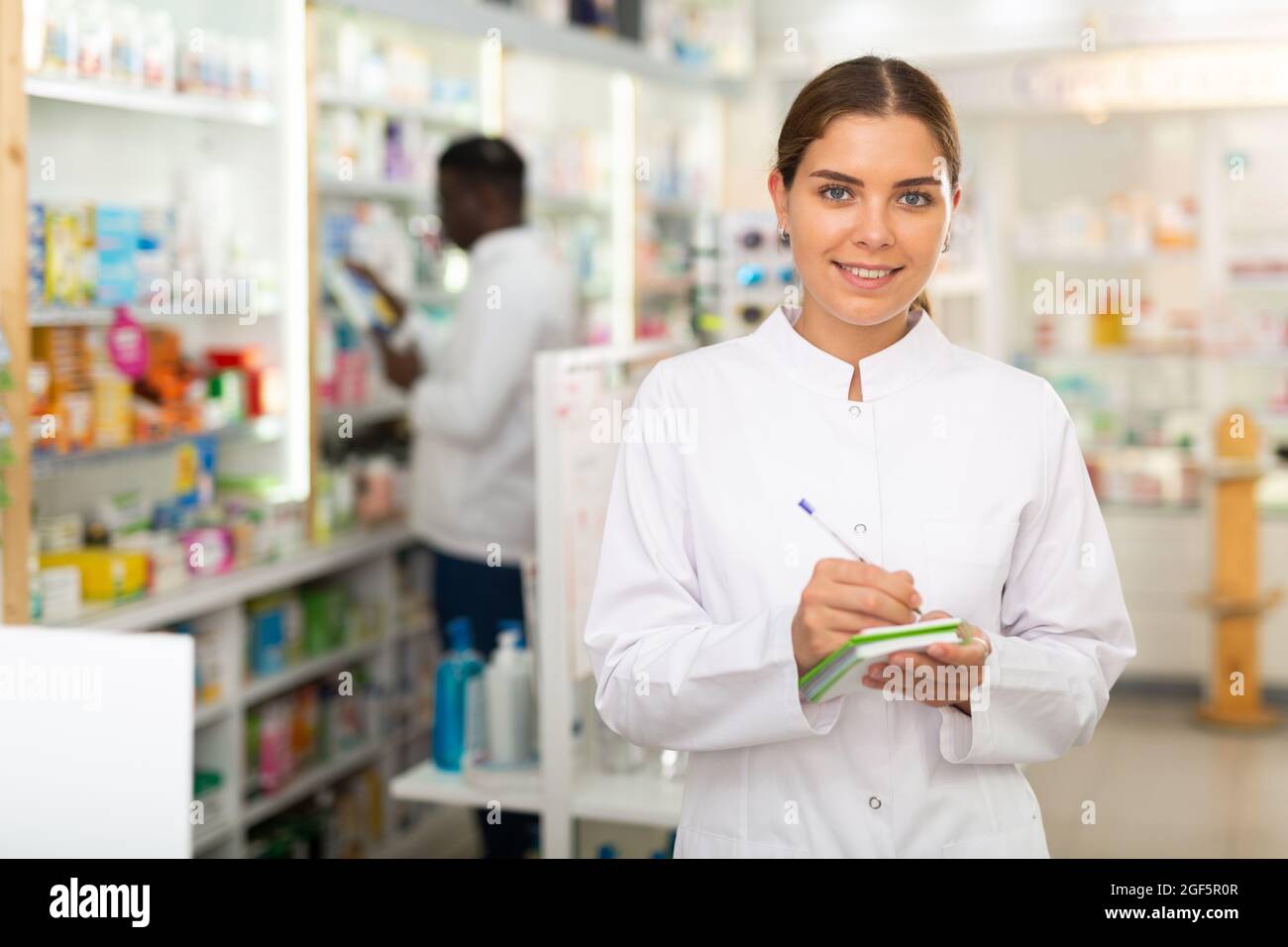 Young smiling female pharmacist making important notes in a notebook ...