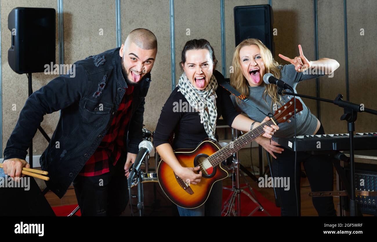 Three bandmates posing together with musical instruments in rehearsal ...