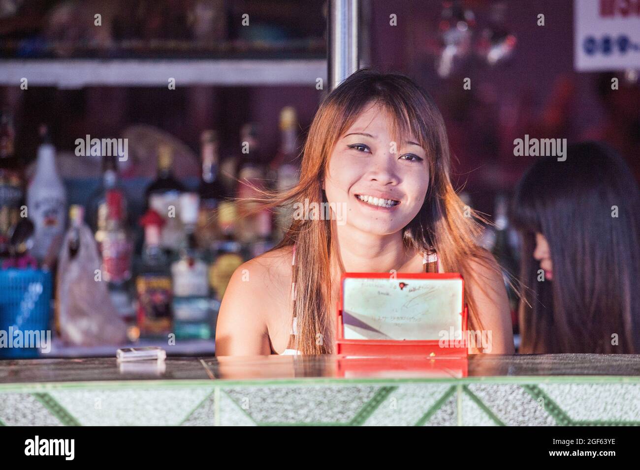 Pretty Thai bar girl sits smiling at counter with vanity mirror in ...