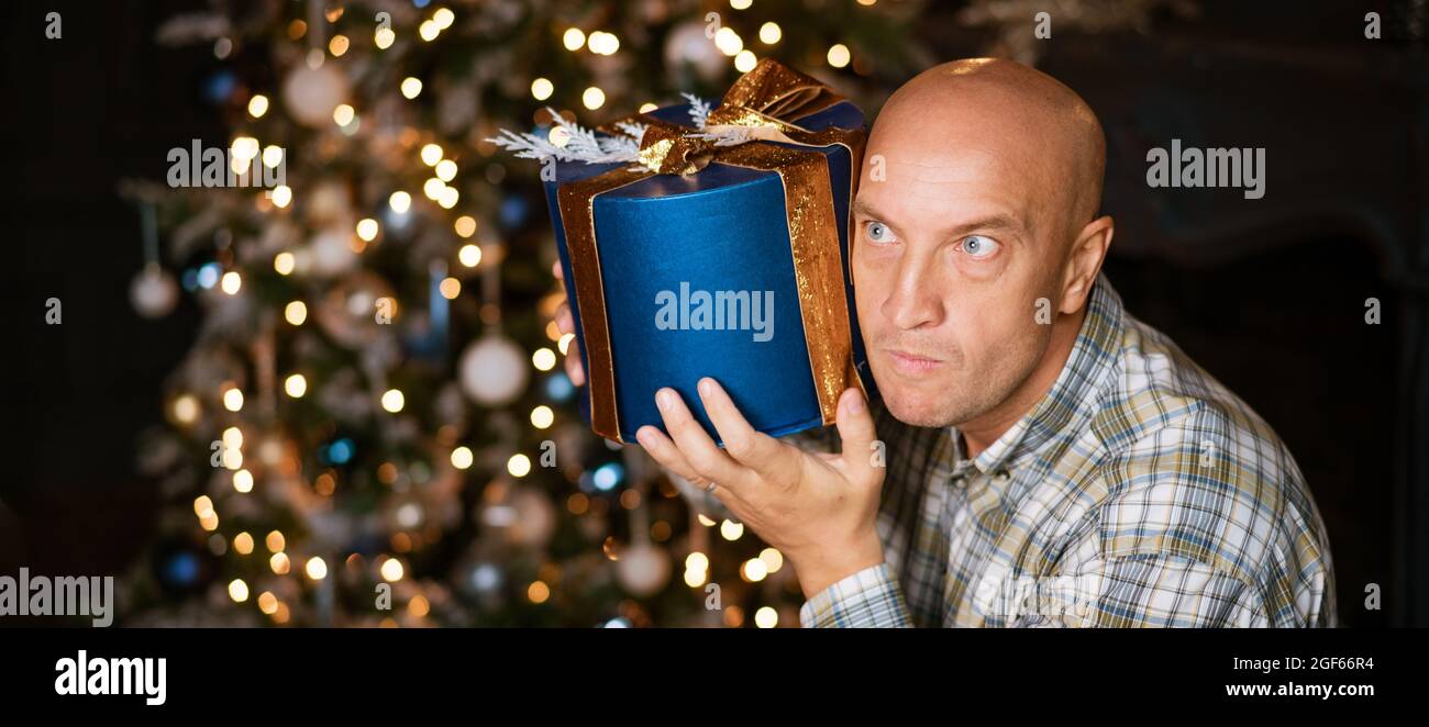 Funny bald man listens to a box with a gift on the background of a ...