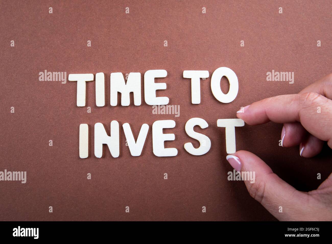Time To Invest. White letters and a man's hand on a brown background ...