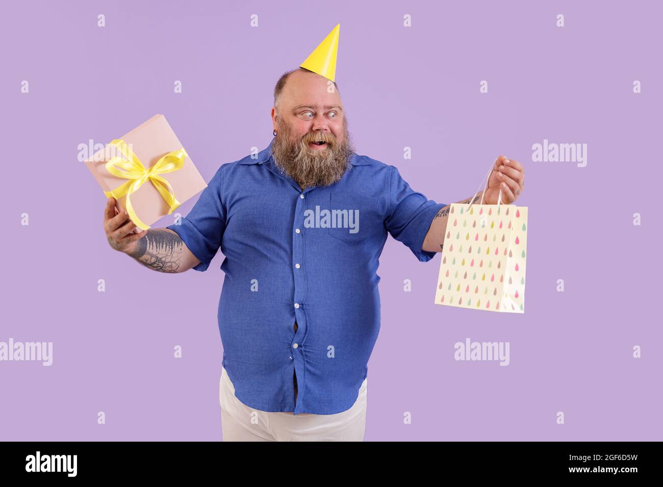 Excited fat man in party hat holds gift and paper bag on purple ...