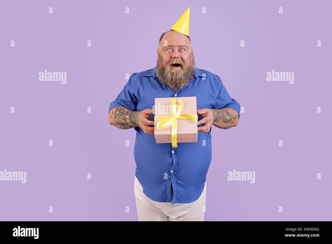 Excited plump man wearing tight shirt holds present on purple ...