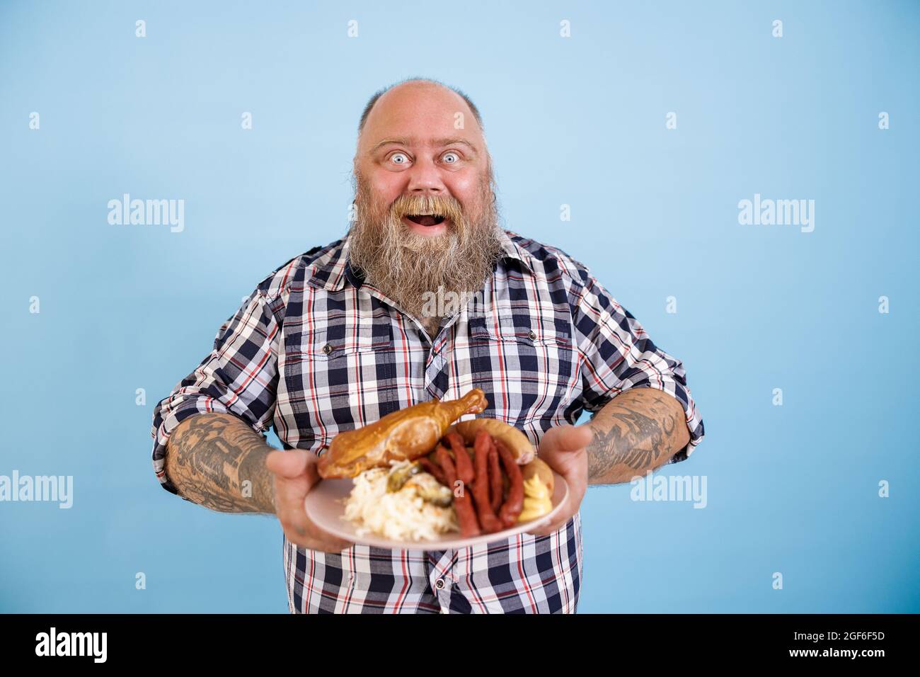 Jouful man with overweight holds plate of rich food standing on light ...