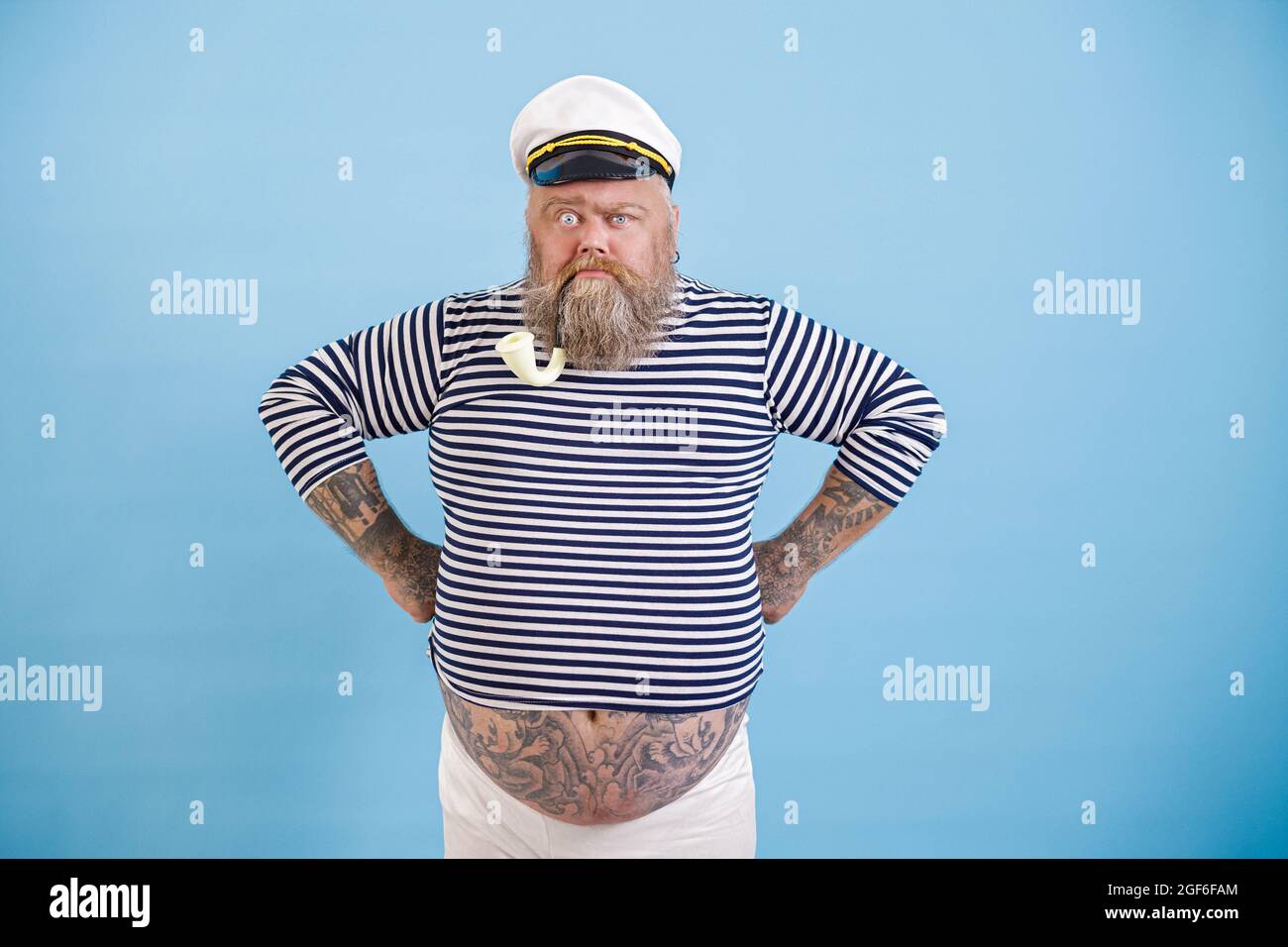 Funny bearded fat man in sailor suit with smoking pipe on light blue ...