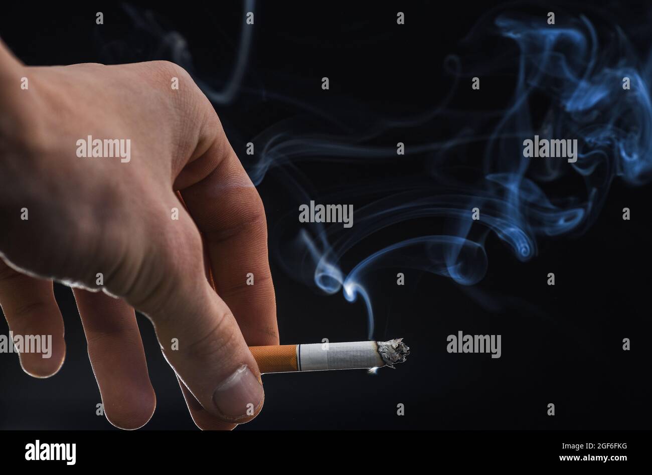 Steaming cigarette with smoke stream in male hand dark background ...